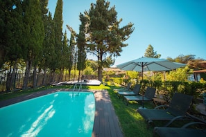 Uma piscina com deck de madeira, espreguiçadeiras e um grande guarda-sol.