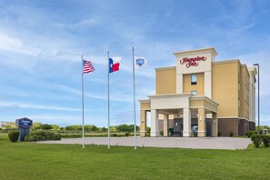 Um hotel Hampton Inn com céu claro, as bandeiras americana e do Texas, e um estacionamento.