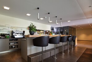 Uma área de bar moderna com balcão, banquetes e uma máquina de café.