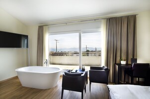 Quarto de hotel moderno com uma banheira grande, uma escrivaninha com cadeira e uma cama.
