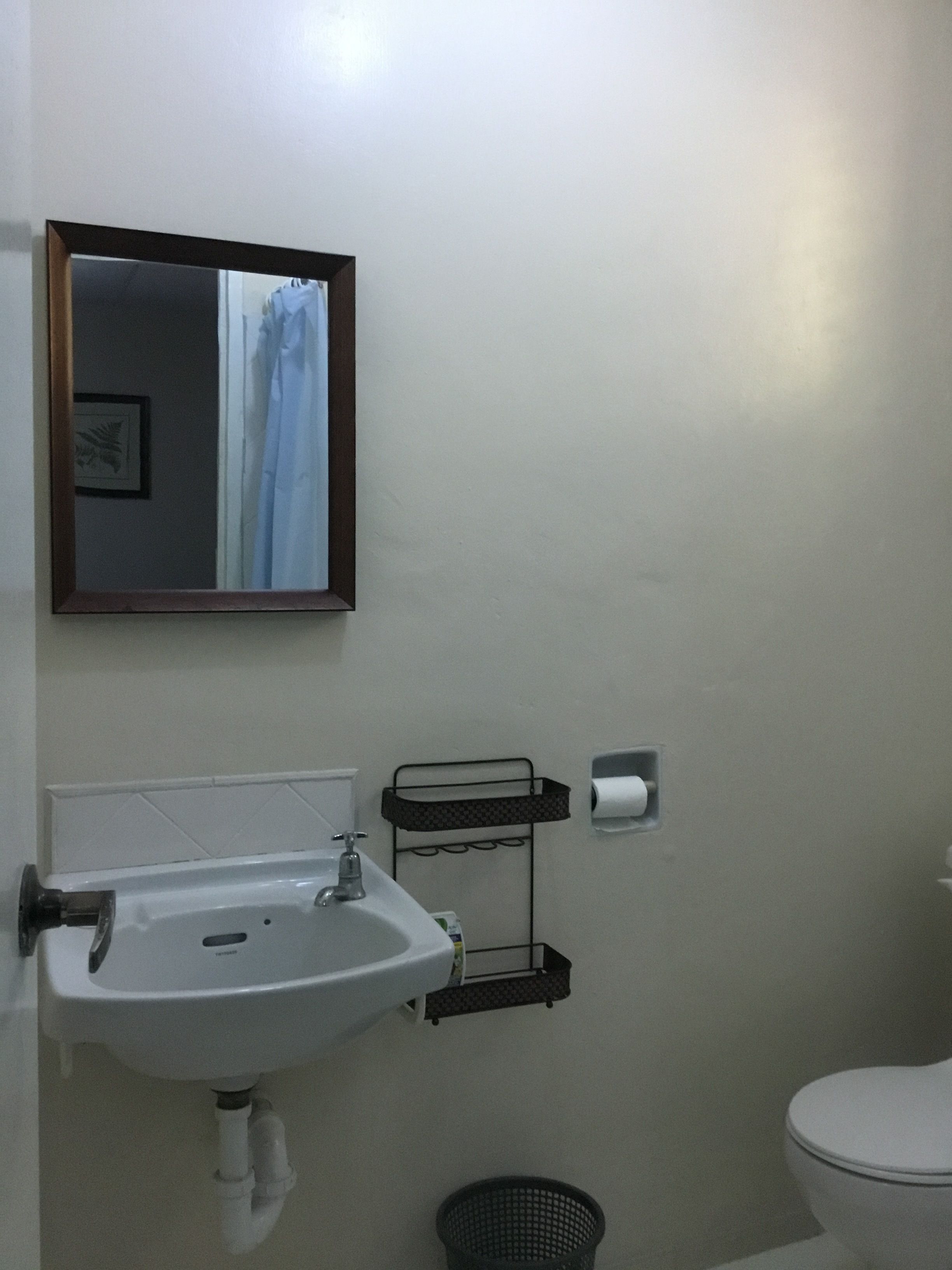 Uma casa de banho com uma pia branca, um espelho, uma sanita e um pequeno contentor de lixo.