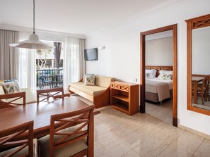 Quarto de hotel moderno com área de refeições, sofá, cama e televisão.