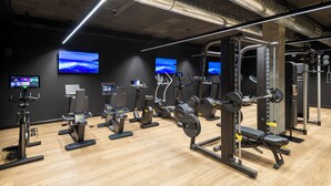 Academia com diversos equipamentos de exercício, incluindo esteiras e estações de musculação, e várias telas exibindo conteúdo de treino.