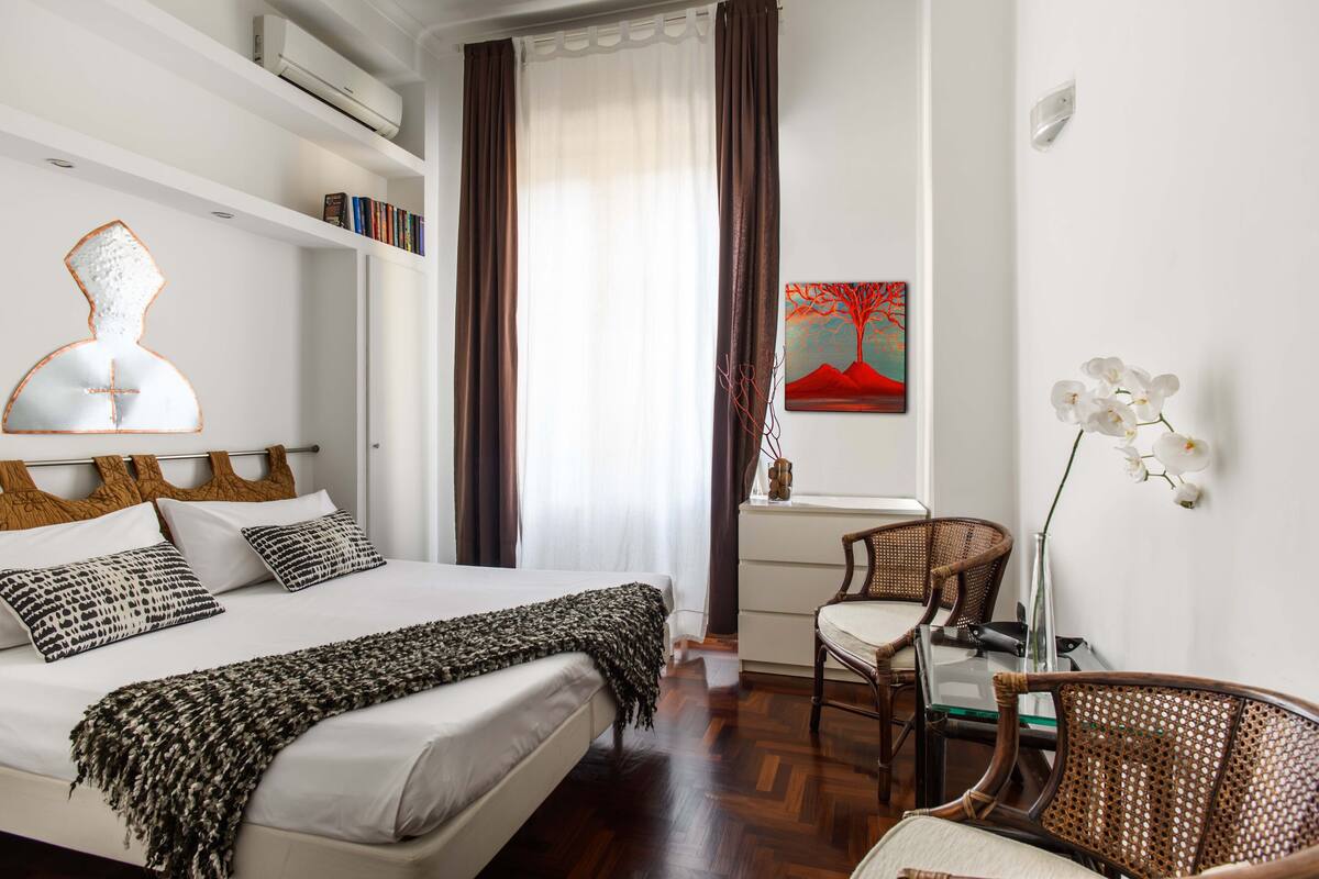 Quarto com cama, mesas de cabeceira, escrivaninha e cadeiras.