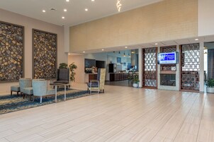 Um saguão de hotel com balcão de recepção, área de estar e uma parede decorativa.