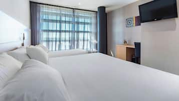 Quarto de hotel com uma cama grande, televisão de tela plana, armário de madeira e janela com cortinas leves.