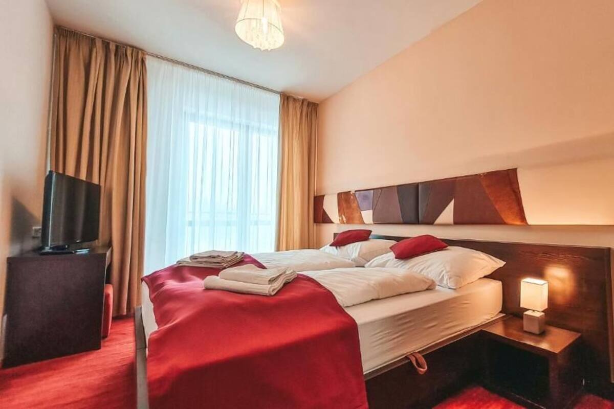 Quarto de hotel com uma cama grande, uma televisão num apoio lateral e uma janela com cortinas.