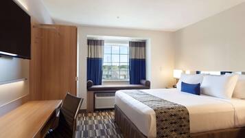 Quarto de hotel com cama, escrivaninha, cadeira, televisão e janela com cortinas.