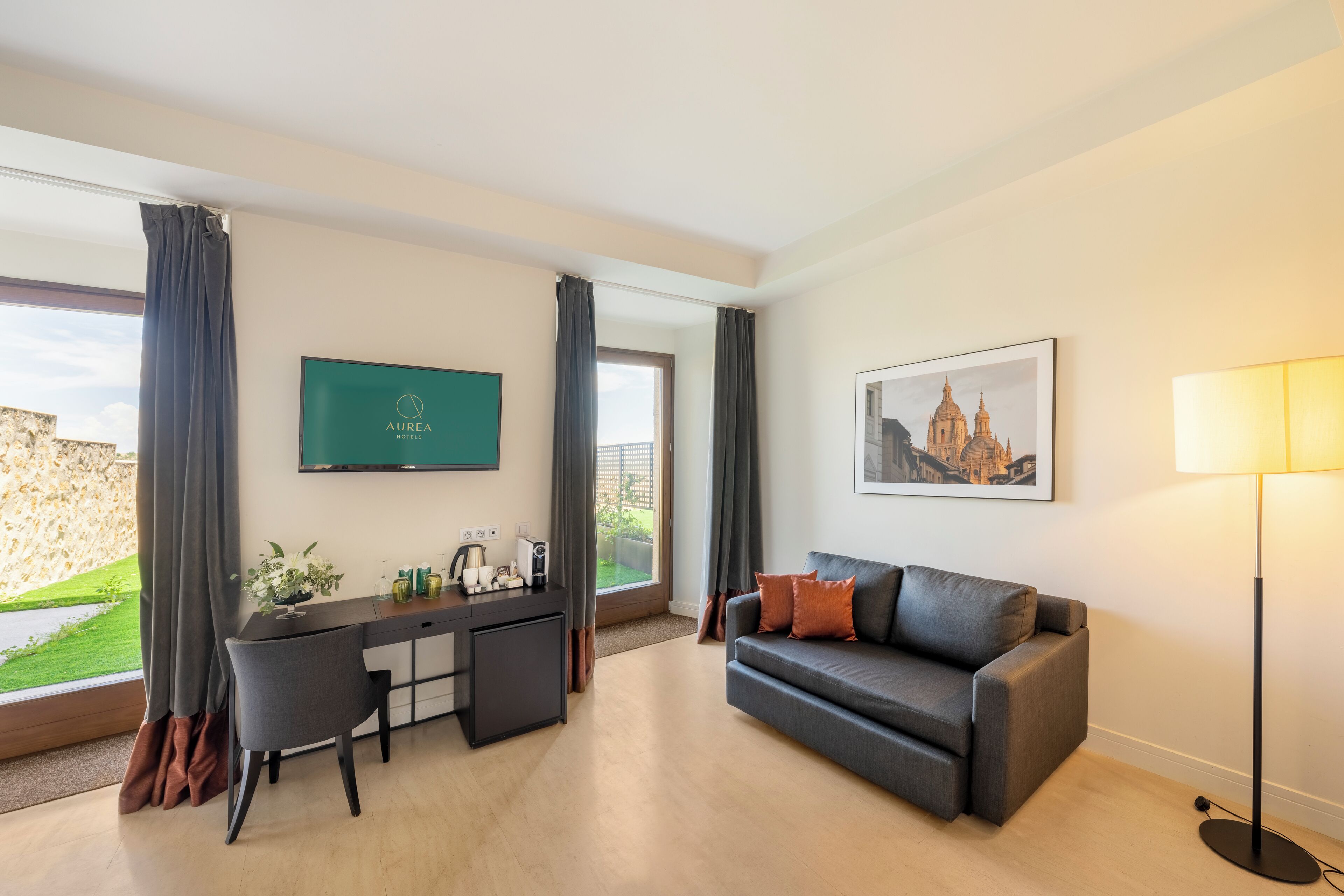 Quarto de hotel moderno com escrivaninha, sofá e TV fixada na parede.