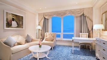 Um quarto com carpete azul estampado, um sofá branco, uma poltrona bege, uma mesa branca e um aparador.