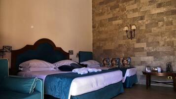 Quarto de hotel com duas camas, cabeceira de madeira, parede de pedra e uma pequena mesa com abajur.