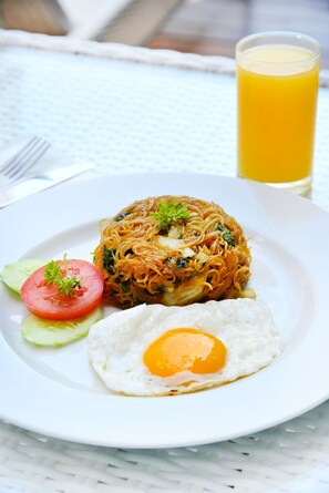 Um prato com macarrão, um ovo frito e um copo de suco de laranja sobre uma mesa.