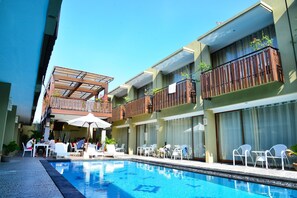 Uma área de piscina com espreguiçadeiras e guarda-sóis, cercada por edifícios altos com varandas.