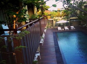 Uma área de piscina com deck de madeira, cadeiras de descanso brancas e uma piscina pequena.