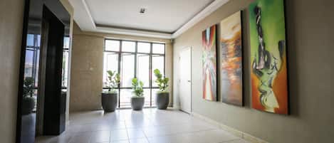 Um corredor amplo com piso de azulejos, janelas grandes e plantas em vasos.