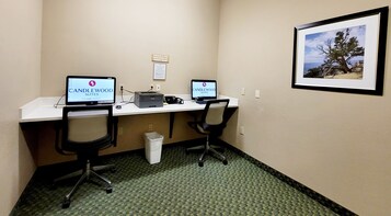 Quarto de hotel com duas mesas, cada uma com um computador exibindo 'CANDLEWOOD SUITES'. Há um quadro na parede e uma lixeira no chão.