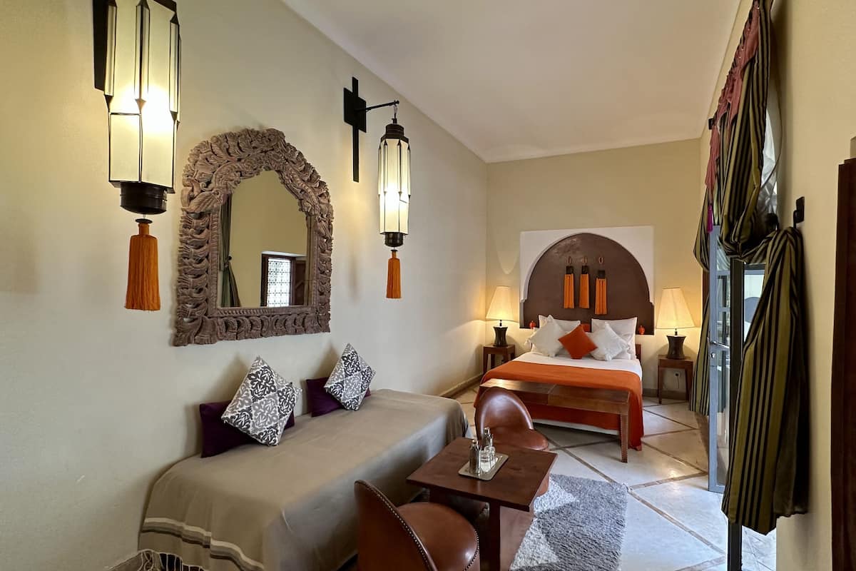 Quarto de hotel com uma cama grande, um sofá, uma mesinha e um espelho.