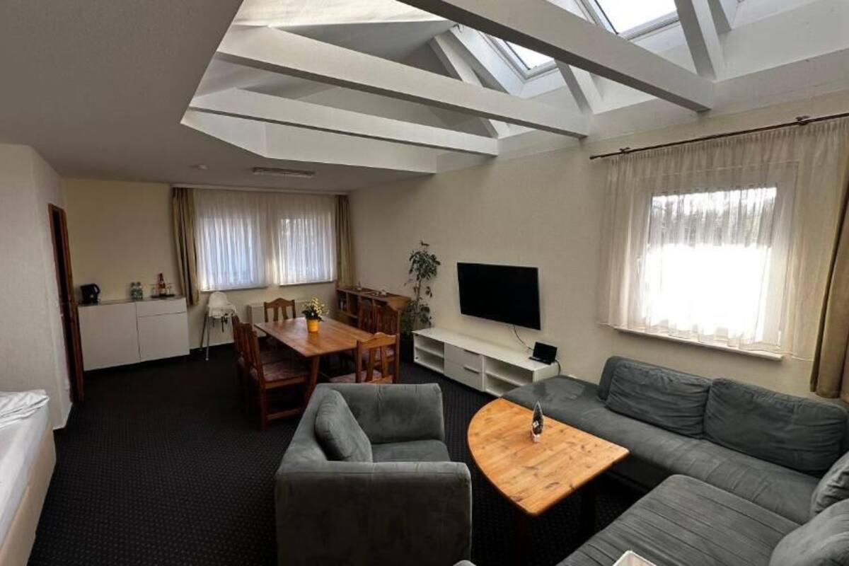 Quarto de hotel compacto com claraboia, sofá, mesa de jantar e televisão.