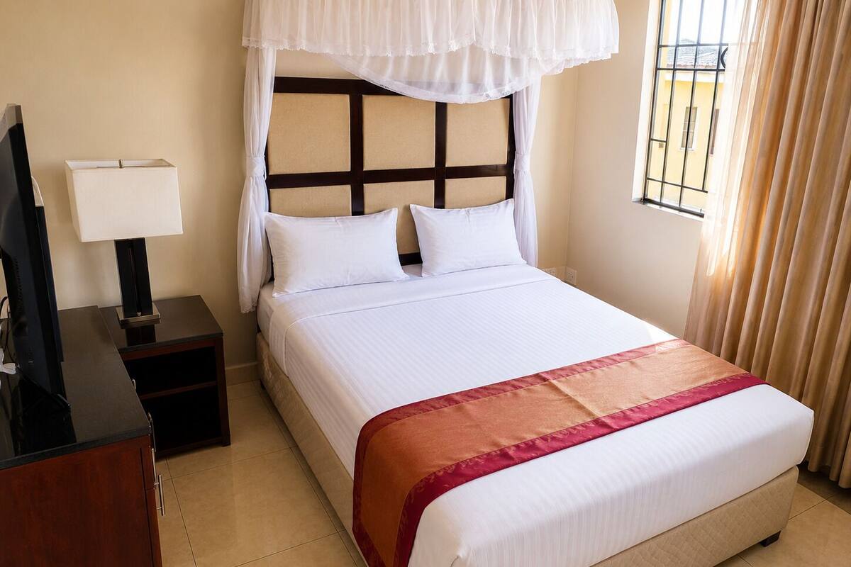 Quarto de hotel com uma cama, televisão, mesa de cabeceira e janela com cortinas.