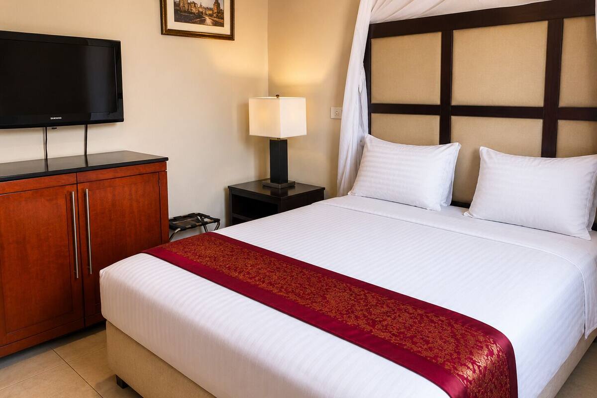 Quarto de hotel com cama, televisão, mesa de cabeceira, abajur e guarda-roupa.