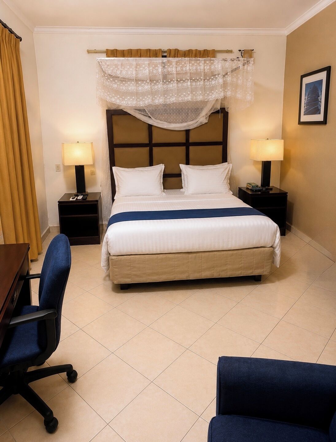 Quarto de hotel com uma cama grande, duas mesas de cabeceira com abajures, uma escrivaninha e uma cadeira.