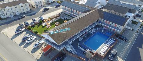 Vista aérea de um hotel com piscina, estacionamento e área externa coberta com guarda-sóis.