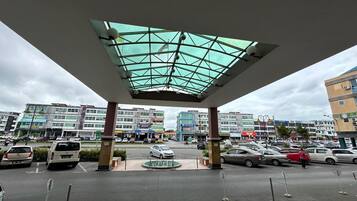 Uma área de estacionamento coberta com teto de vidro, vários carros e diversos edifícios ao fundo.