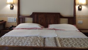 Uma cama de casal com peseira de madeira, duas mesas de cabeceira com luminárias e um edredom estampado com motivos florais.