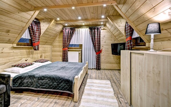 Quarto sótão aconchegante com cama, televisão e paredes de madeira.