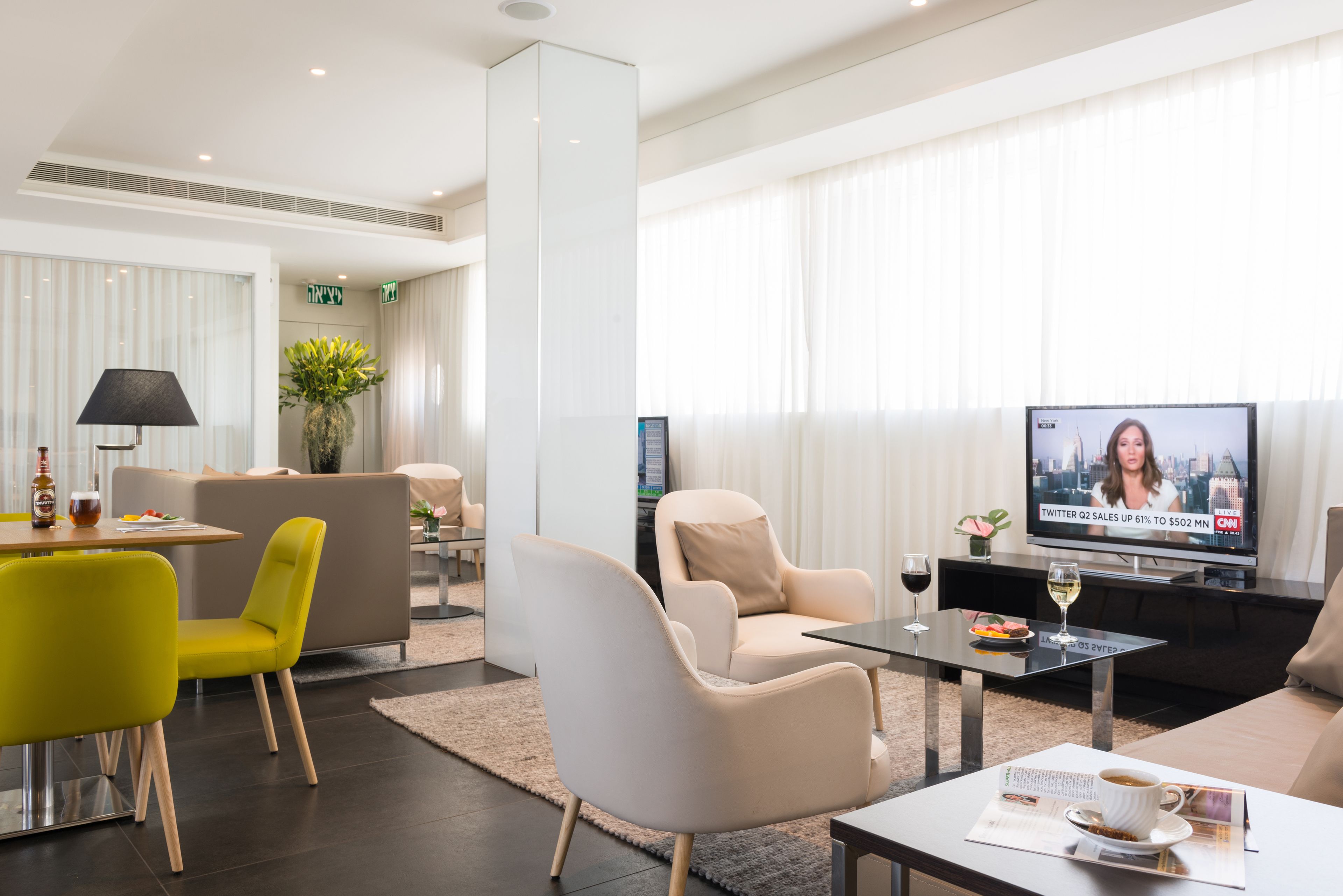Uma sala de estar moderna com sofá, poltronas, mesa de centro e uma televisão exibindo um canal de notícias.