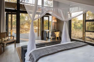 Quarto com uma cama grande, escrivaninha e cadeira, tudo em design moderno e aberto, com janelas amplas.