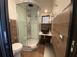 Casa de banho moderna com cabine de duche em vidro, sanita branca e lavatório com cuba preta.