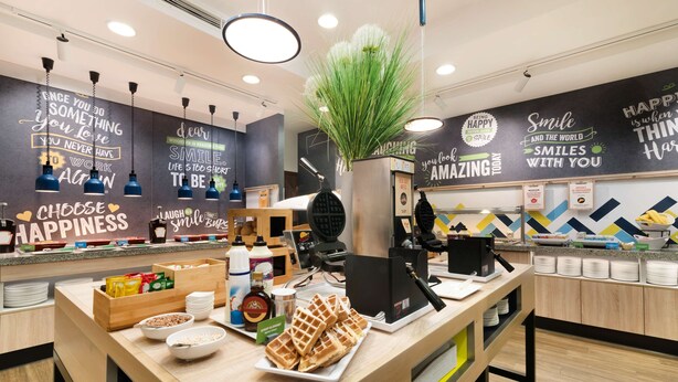 Um café moderno com um balcão exibindo waffles e itens de café da manhã, arte motivacional na parede e uma disposição limpa e organizada.