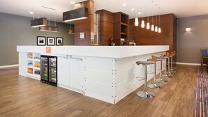 Uma área de bar moderna com balcão branco, banquetes de aço inoxidável e iluminação pendente.