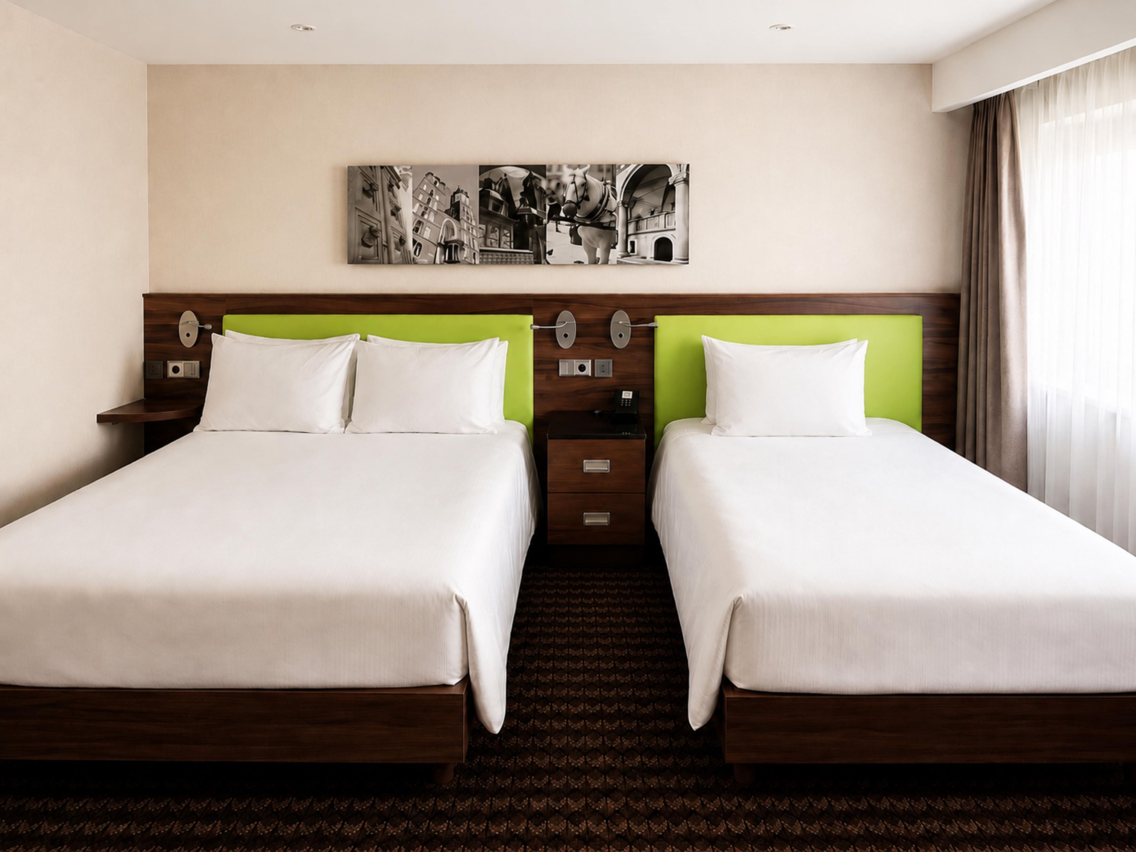 Quarto de hotel com duas camas, uma mesa de cabeceira, um telefone e uma obra de arte pendurada na parede.