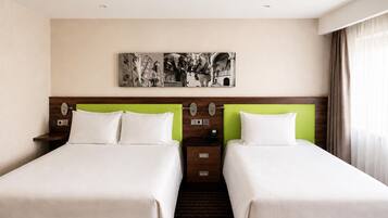 Quarto de hotel com duas camas, uma mesa de cabeceira, um telefone e uma obra de arte pendurada na parede.