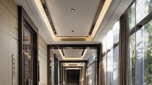 Um corredor de hotel moderno, com layout longo e reto, grandes janelas de um lado e teto com iluminação embutida.