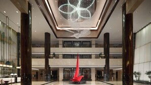 Um hall espaçoso com uma escultura vermelha central, um detalhe de teto floral iluminado e um chão de mármore polido.