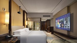 Quarto de hotel com uma cama grande, mesas de cabeceira, uma escrivaninha e um pôster grande na parede.