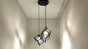 Um corredor com um moderno candeeiro geométrico, uma escada e um extintor de incêndio.