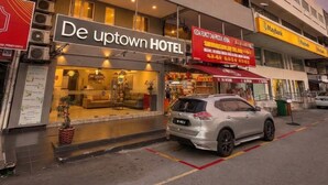 Um hotel com uma placa que diz "De Uptown Hotel" e uma agência do Maybank.