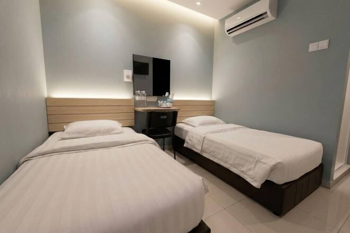 Quarto de hotel com duas camas, uma escrivaninha pequena, um espelho e um ar condicionado.