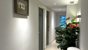 Um corredor com piso ladrilhado, um quadro na parede e um vaso de planta.