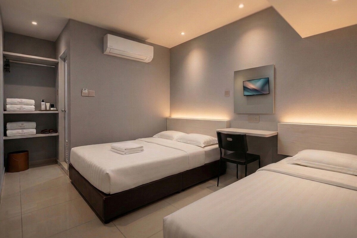 Quarto de hotel com duas camas, uma escrivaninha, uma cadeira, ar condicionado e televisão na parede.
