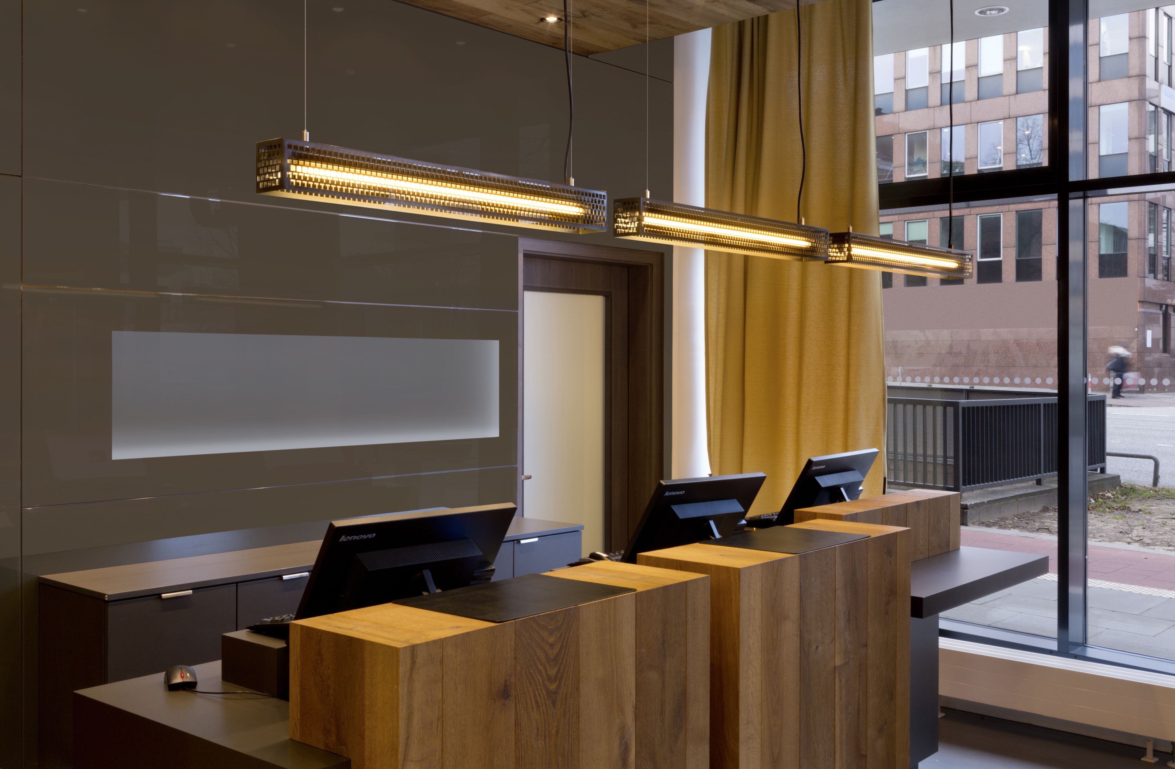 Balcão de recepção com design moderno, grandes janelas com vista para a cidade e um lustre pendurado acima.