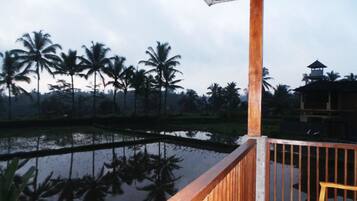 Um deck de madeira com guarda-corpo, com vista para um lago e palmeiras ao fundo.
