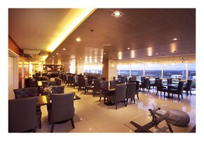 Um amplo saguão de hotel com várias áreas de estar, um bar e grandes janelas com vista para a cidade.