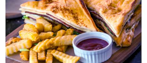 Sanduíche grelhado com batatas fritas e ketchup sobre uma tábua de madeira.