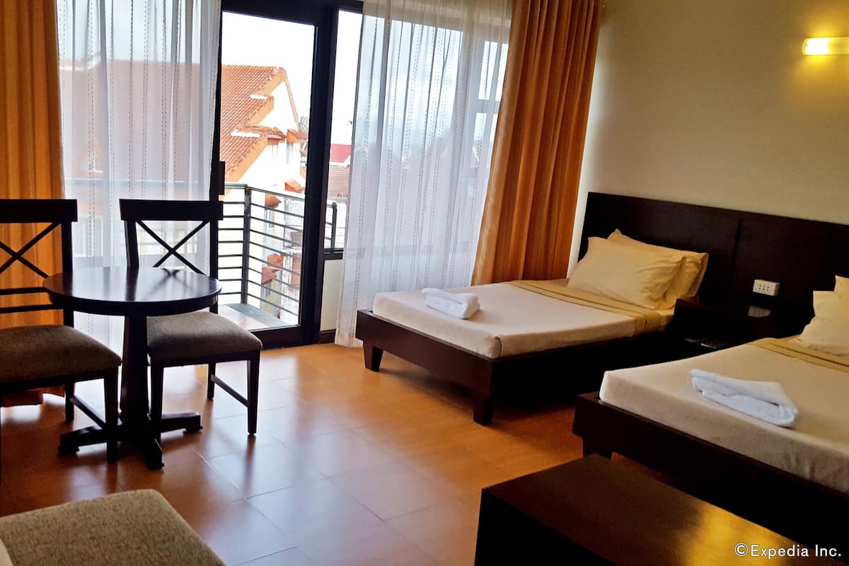Quarto de hotel com uma cama, escrivaninha, cadeira e uma mesinha. Há uma janela com cortinas.