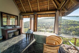 Casa de banho com uma banheira grande, toucador com espelho e vista para uma paisagem montanhosa.